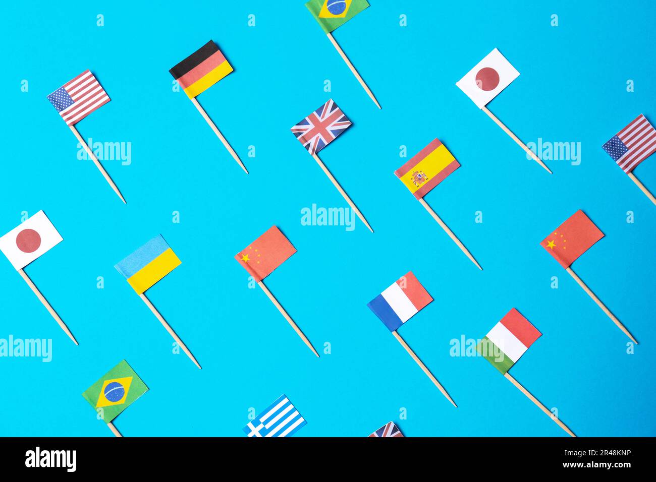 Many small paper flags of different countries on light blue background ...