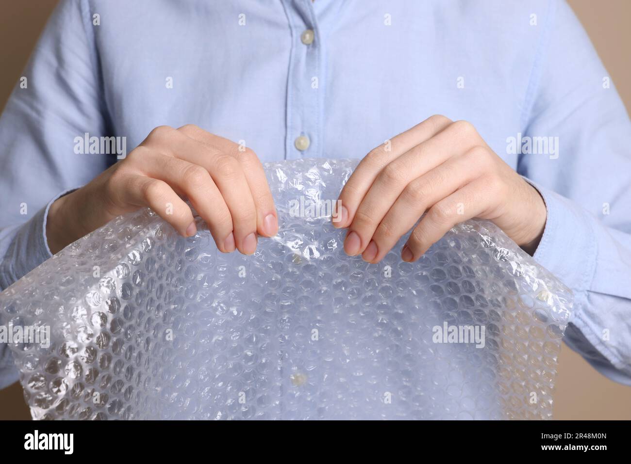 Woman popping bubble wrap on beige background, closeup. Stress relief ...