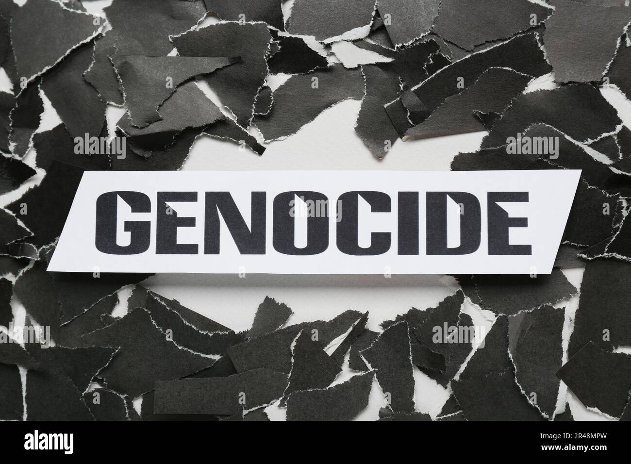 Card with word Genocide and pieces of torn black paper on white ...