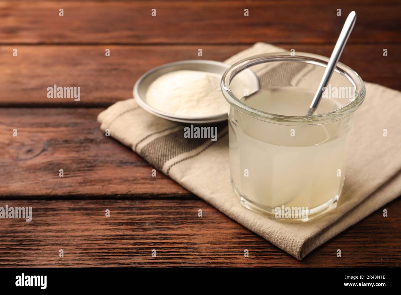 Glass of agar-agar jelly and bowl with powder on wooden table. Space ...
