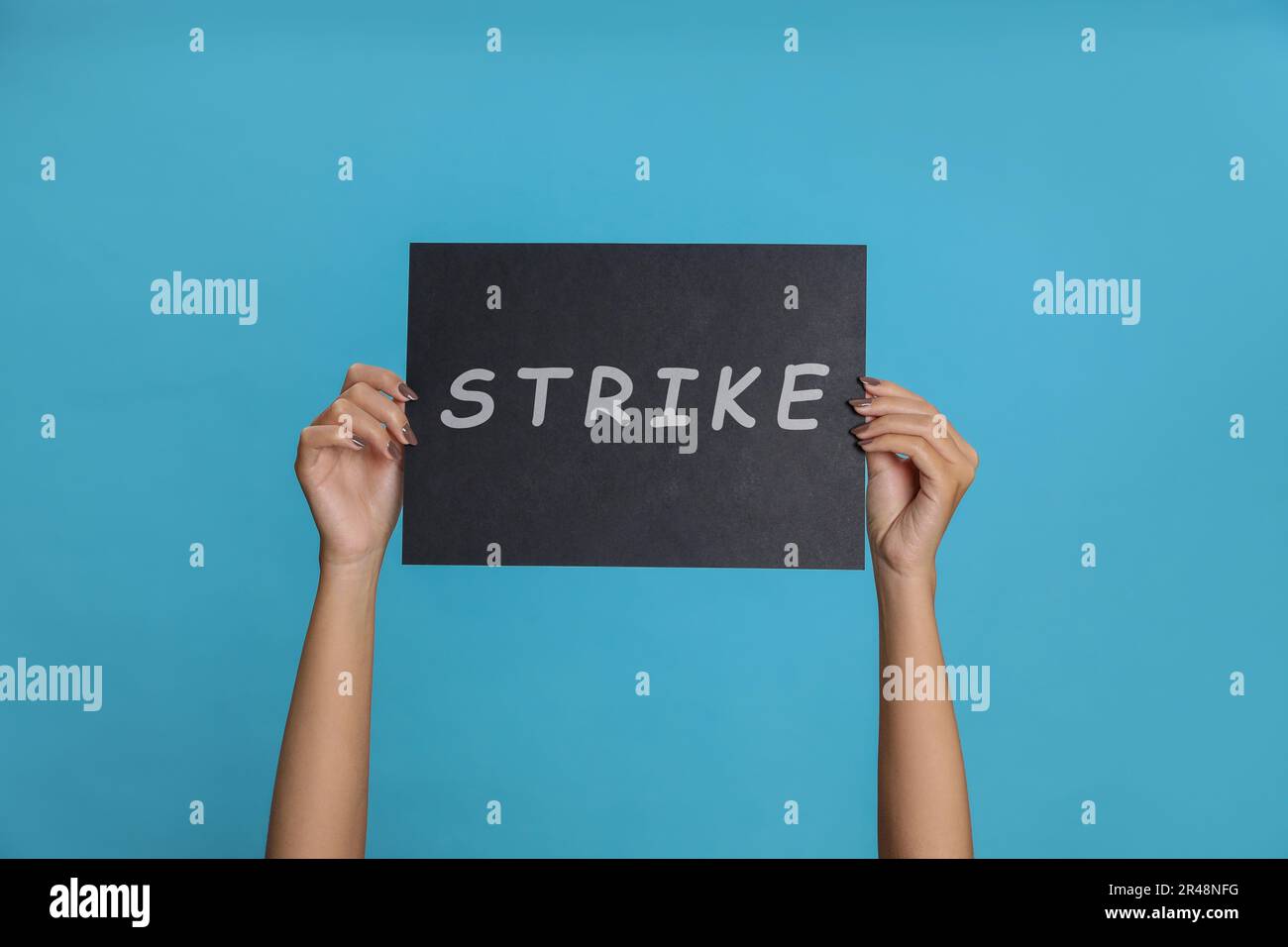 Woman holding sign with word Strike on light blue background, closeup ...
