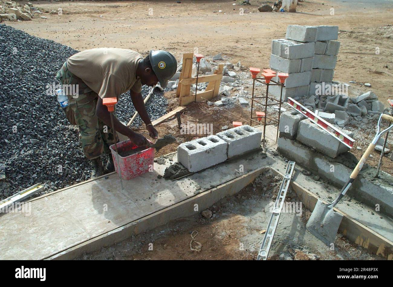 US Navy Seabee places the first course of masonry block for a ...