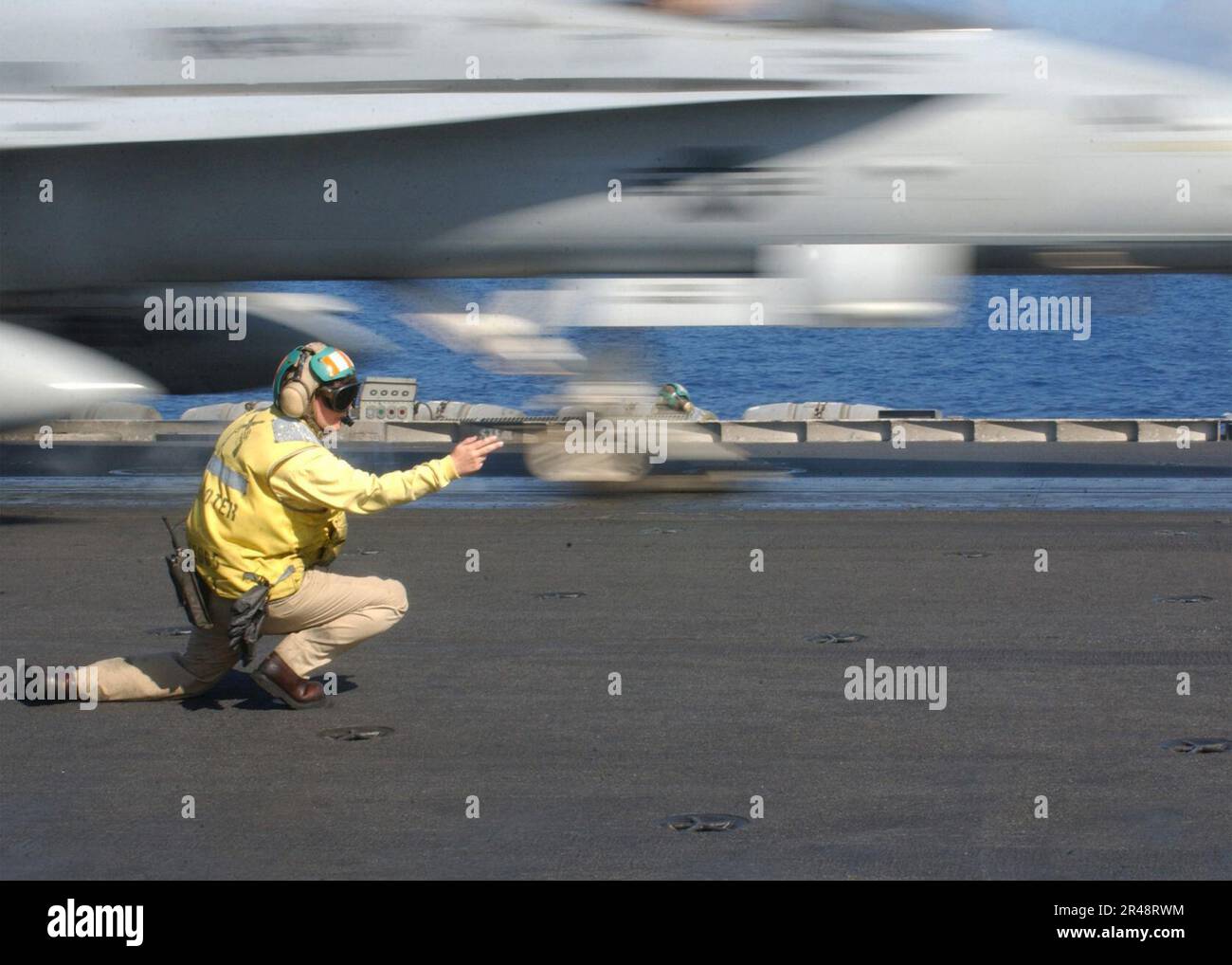US Navy Flight deck handler signals launch of an F-A-18 Hornet from the ...