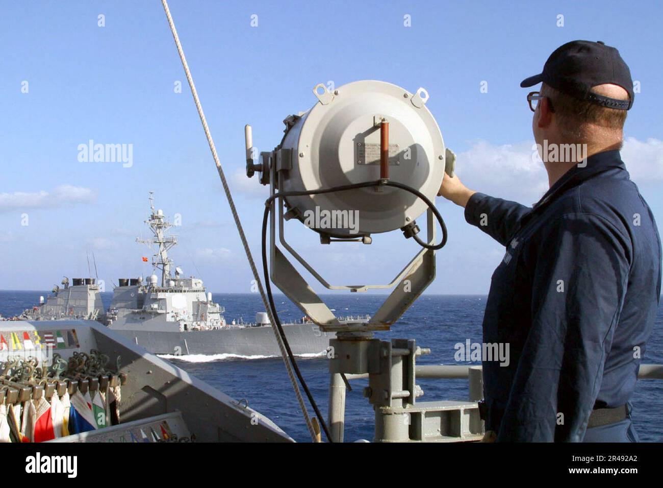 US Navy Signalman 1st Class uses a signal light to communicate with the ...