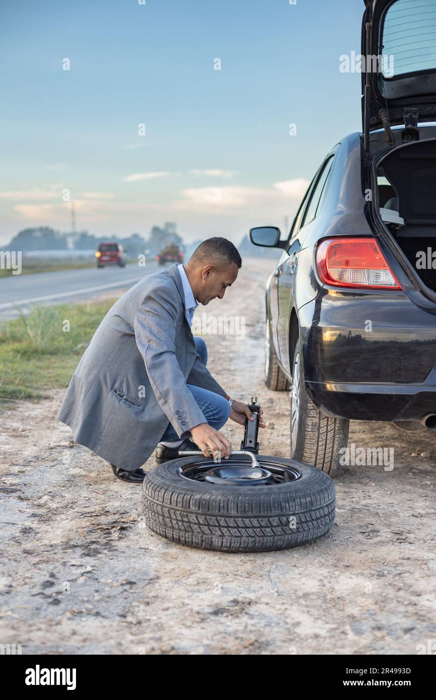 Latino man changes a flat tire on his car at the side of the road Stock ...