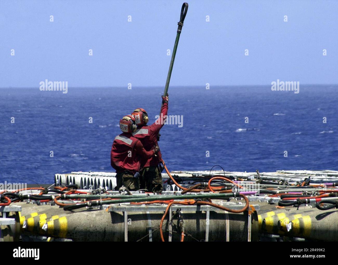 US Navy Aviation Ordnancemen wait to hook up a pallet of bombs to an ...