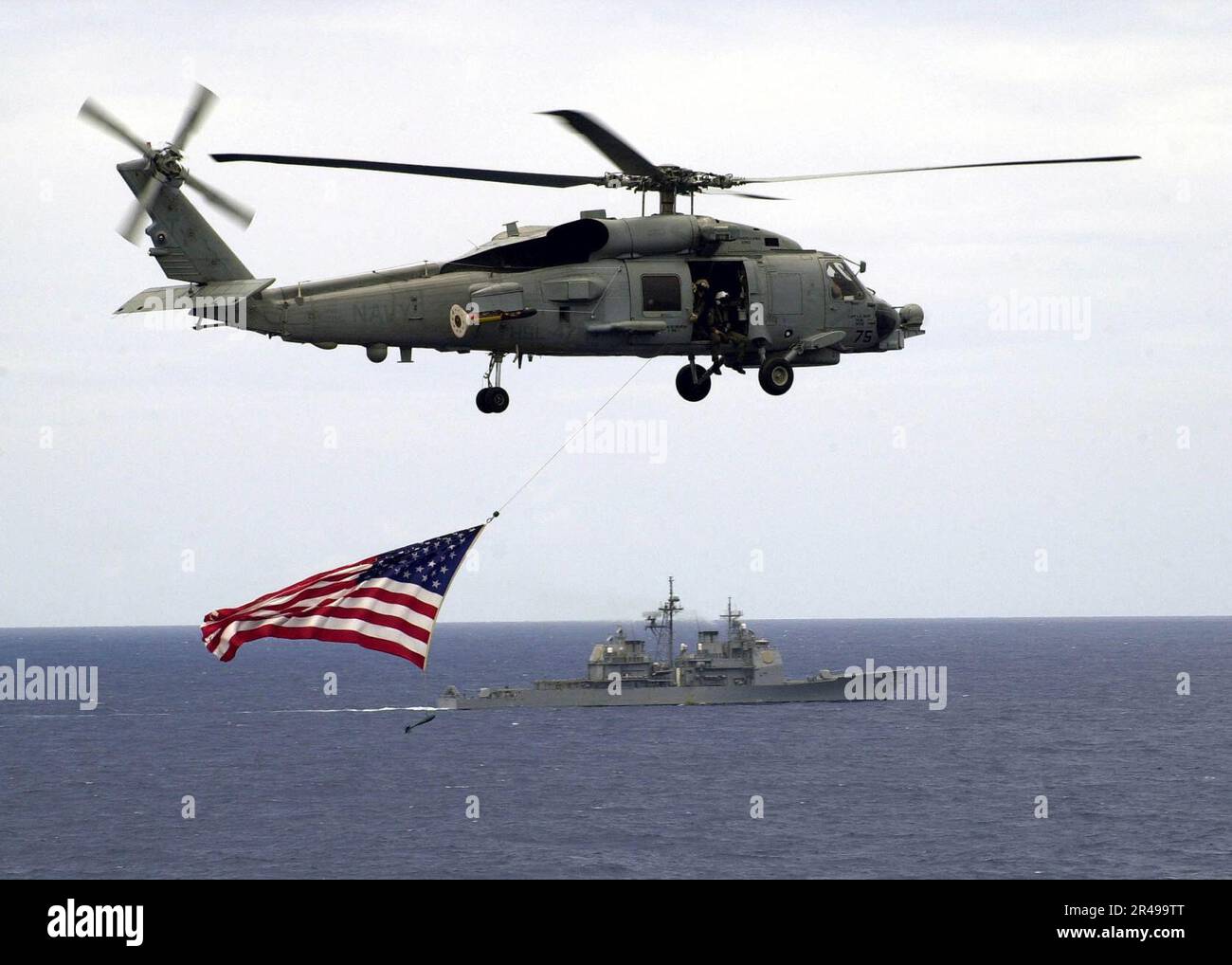 US Navy An SH-60F Seahawk helicopter flies an American flag between the ...