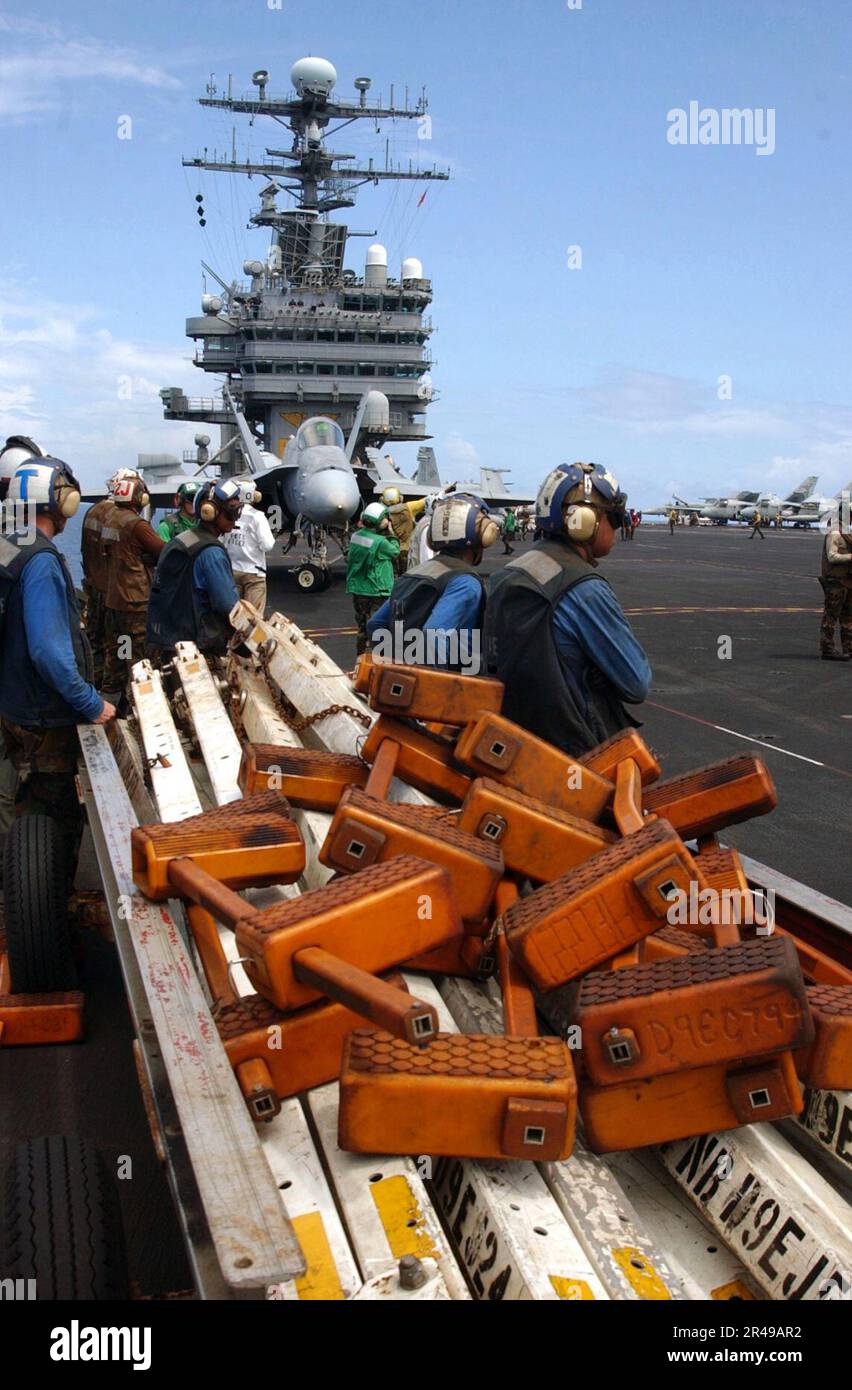 US Navy Flight deck personnel stand near aircraft tow bars and chocks ...