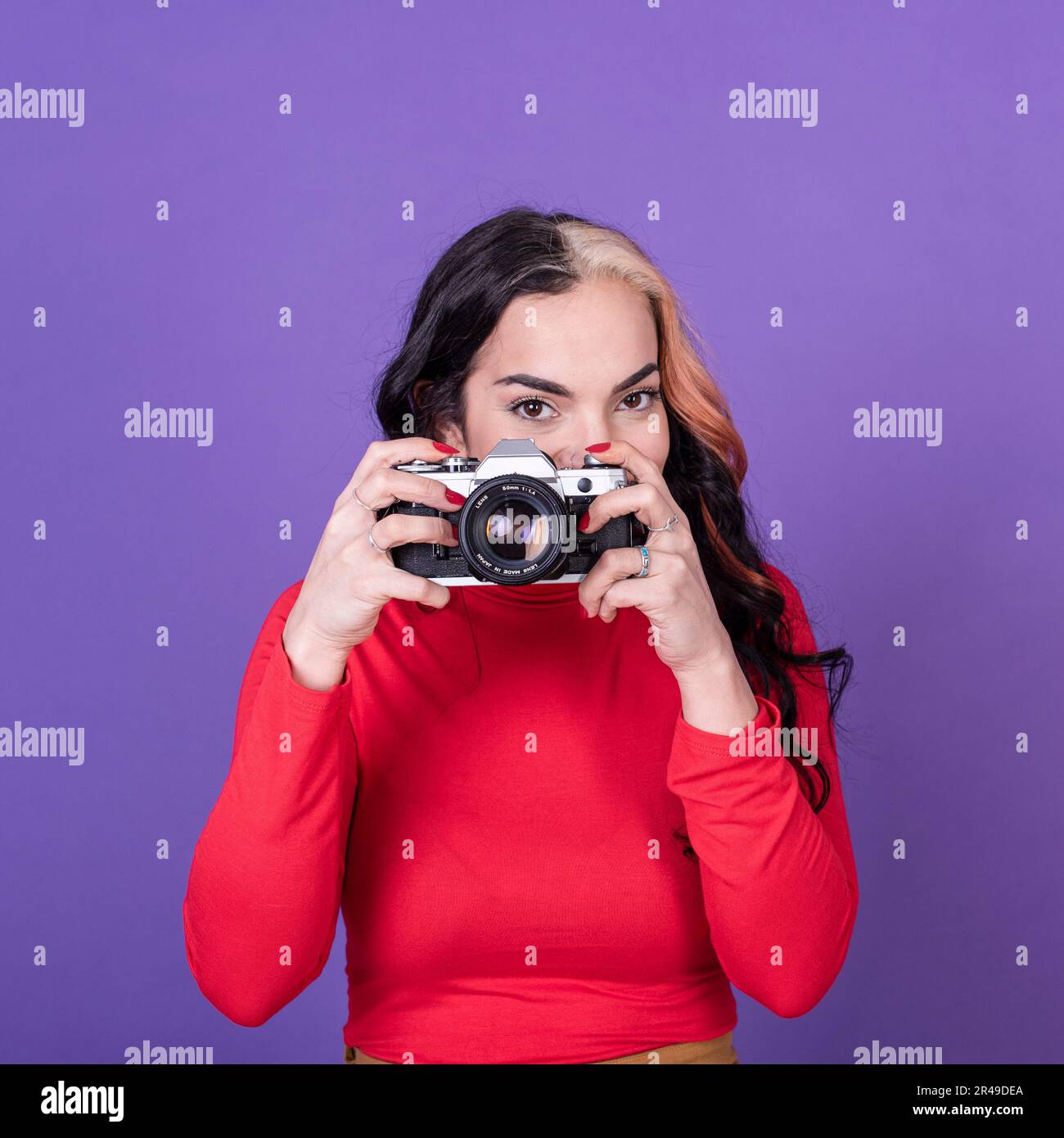 Attractive young lady taking a photo with her film camera over a violet ...