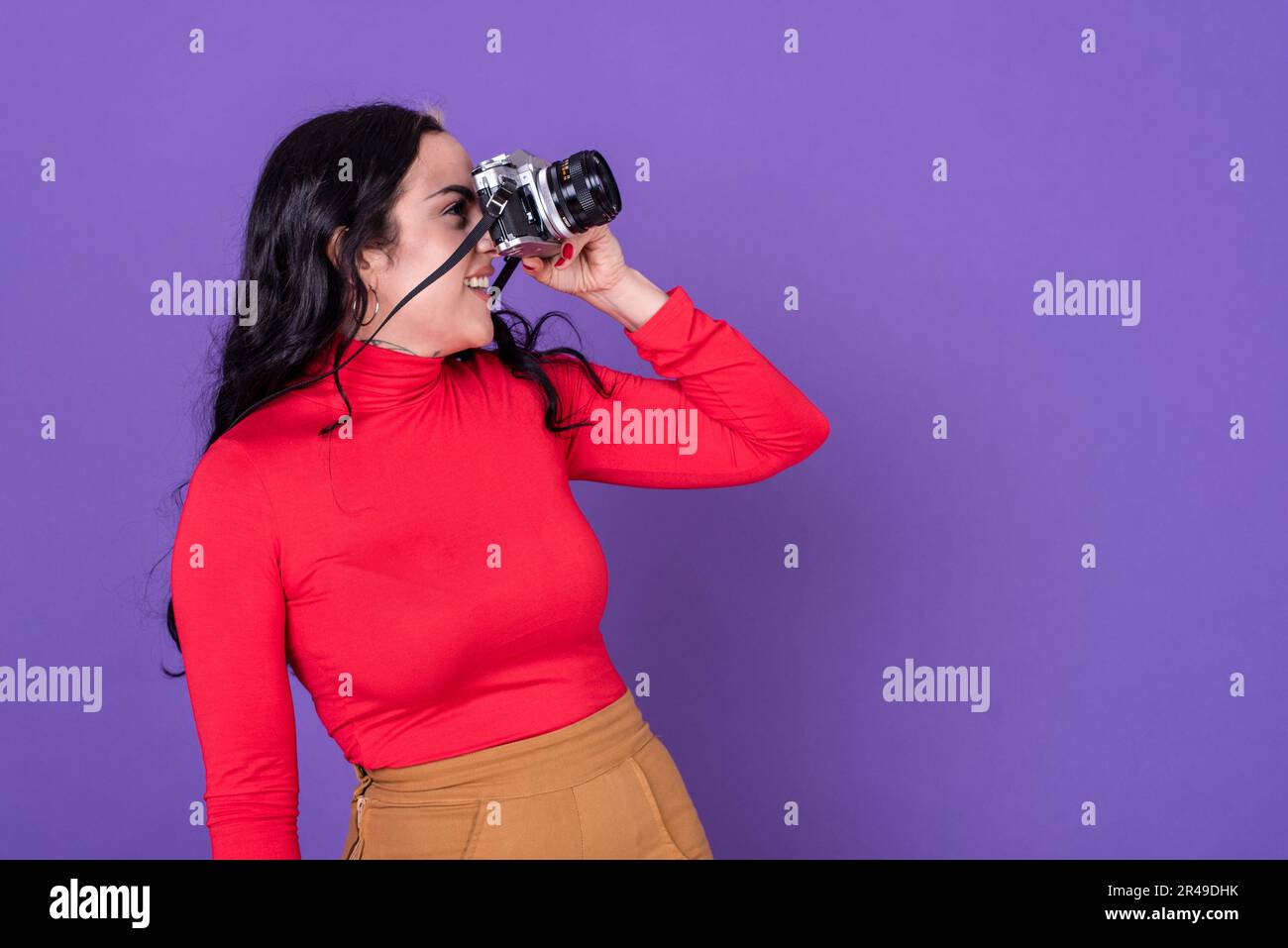 Attractive young lady taking a photo with her film camera over a violet ...