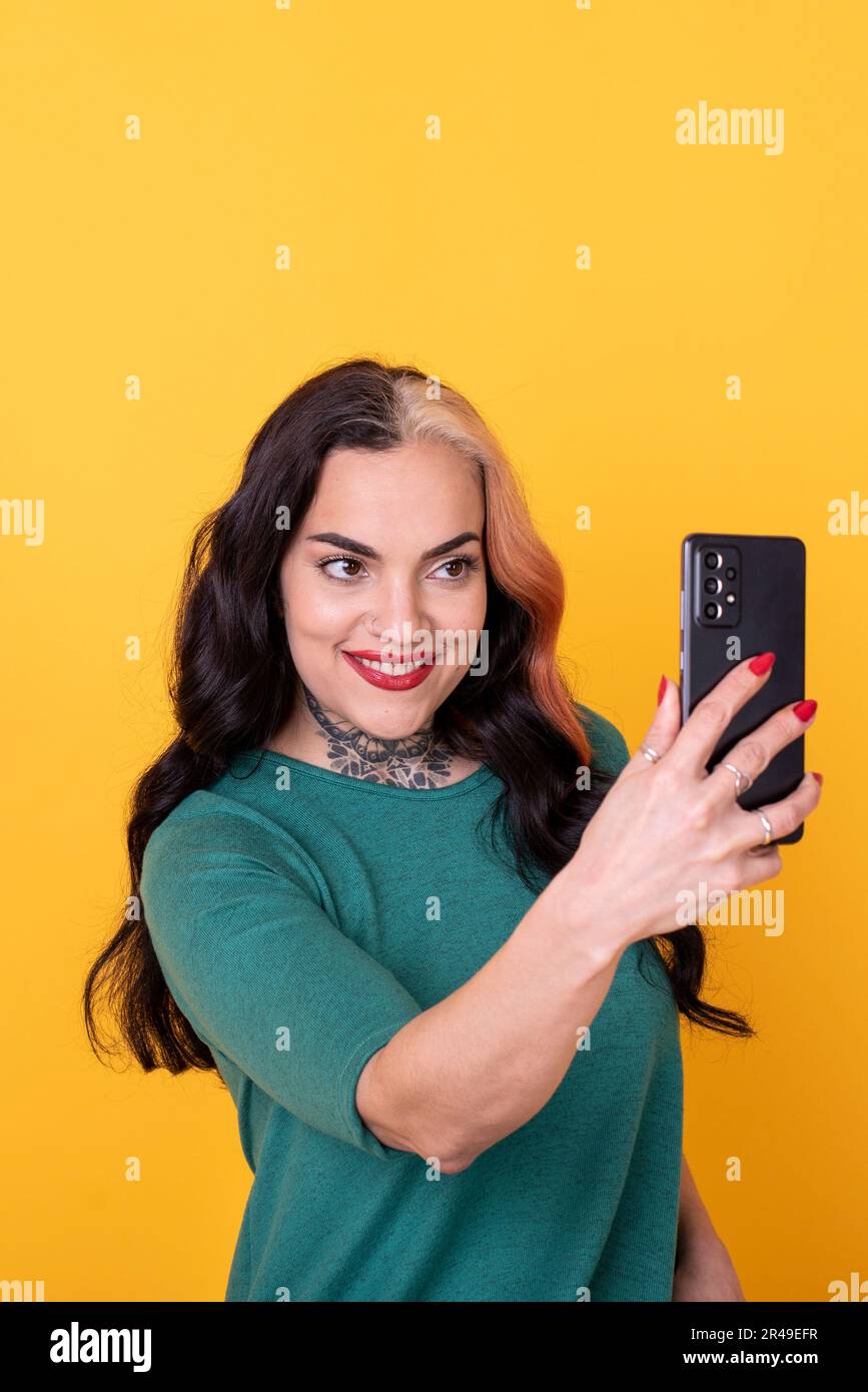 Portrait of an attractive woman making a selfie over yellow background. Studio shot Stock Photo ...