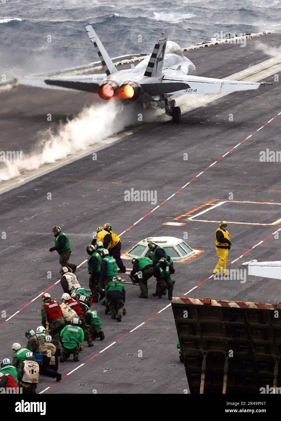 US Navy Flight deck personnel kneel between the foul lines as an F-A ...