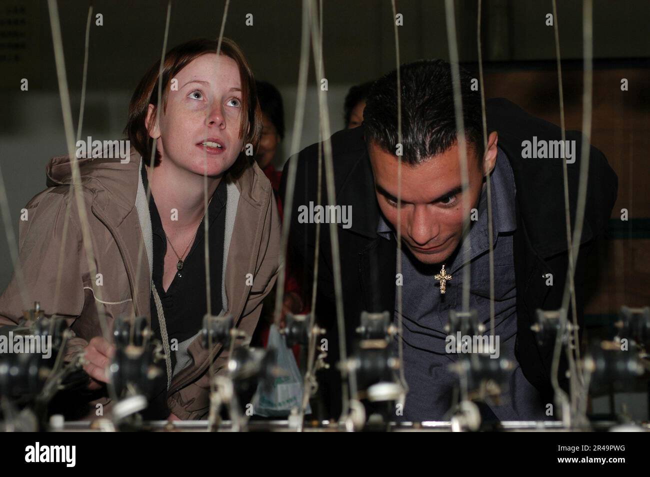 US Navy Sailors closely watch a machine separate strands of silk from a ...