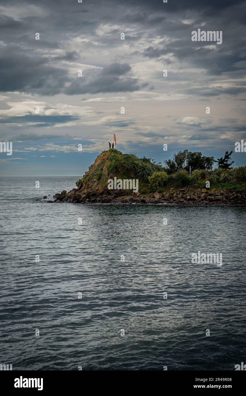 A vertical shot of a rocky cliff with people over the water in New ...