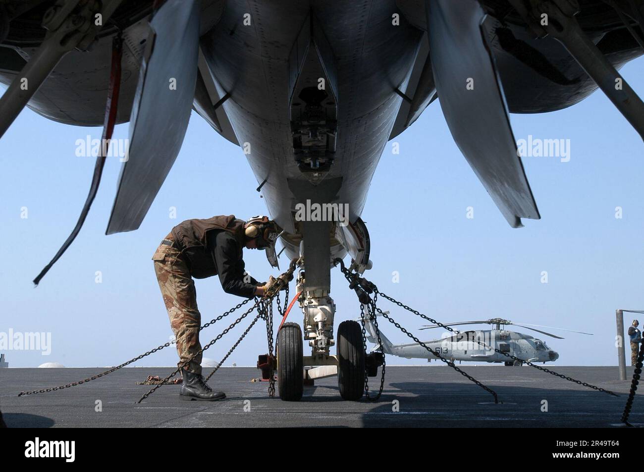 US Navy Plane Captain tightens a tie-down chain on an F-A-18C Hornet ...
