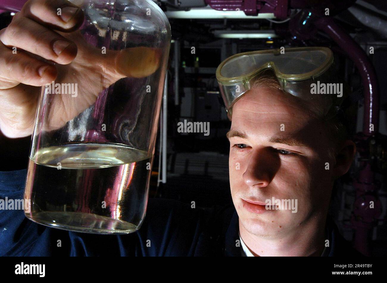 US Navy Airman inspects a sample of JP-5 aviation fuel in a pump room ...