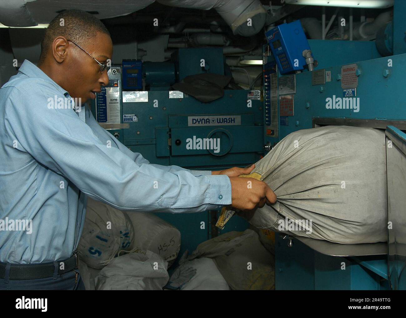 US Navy Airman Recruit unloads laundry from a washer in the ship's ...