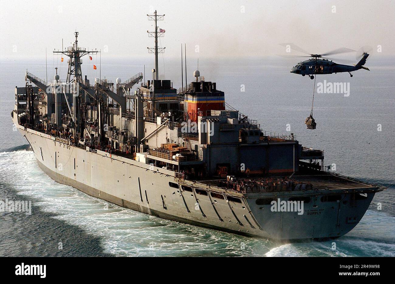 US Navy A MH-60S Knighthawk conducts a vertical replenishment at sea with the Military Sealift ...