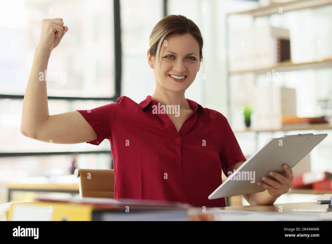 Cheerful woman shows arm muscles holding clipboard Stock Photo - Alamy