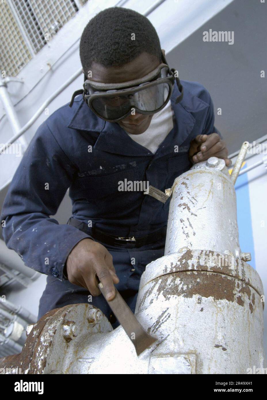 US Navy Seaman chips away old paint from pipes in preparation for ...