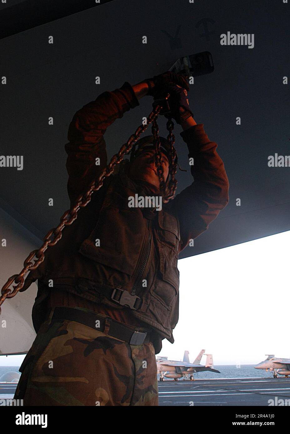 US Navy Aviation Support Equipment Technician Airman secures a tie-down ...