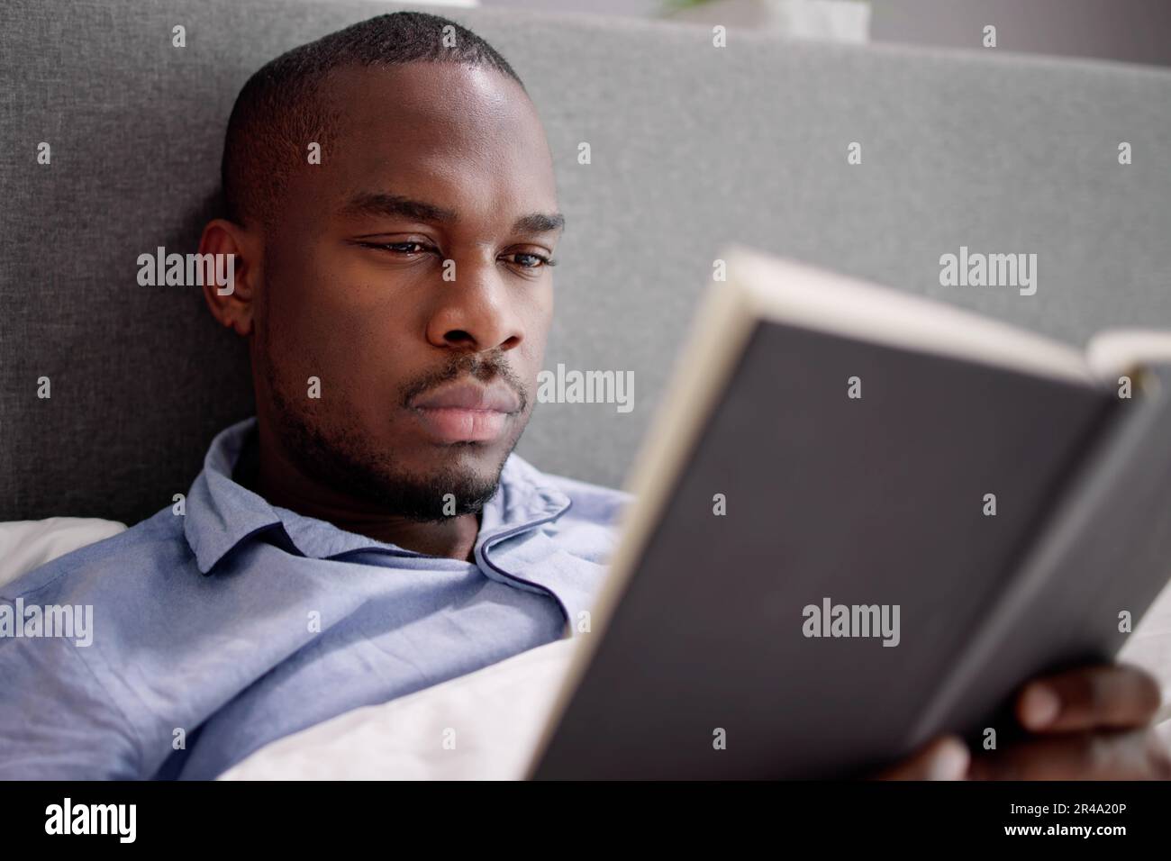 Happy Young African Man Reading His Book On Bed Stock Photo - Alamy