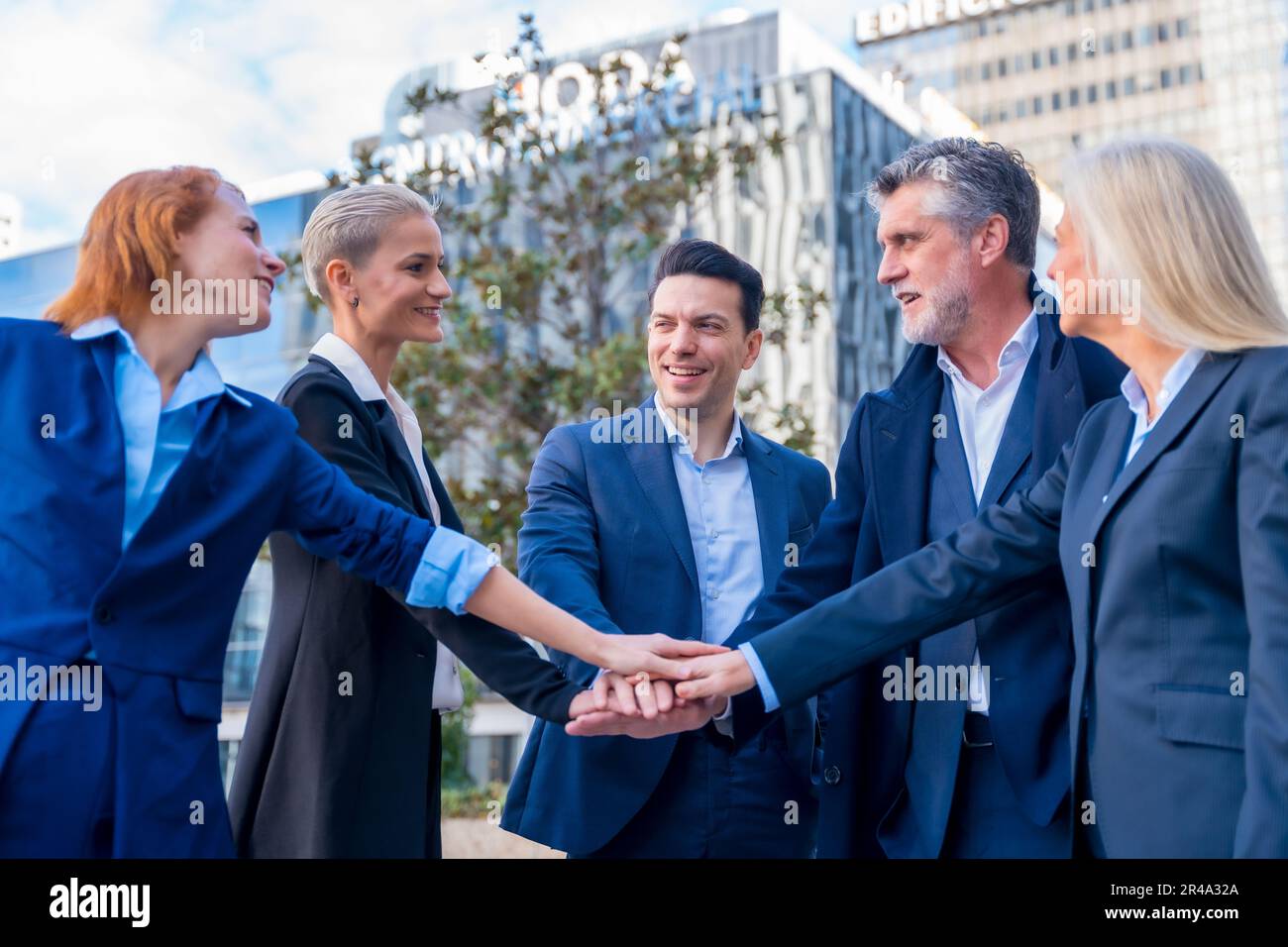 Five accomplished business people are standing in a circle with their ...