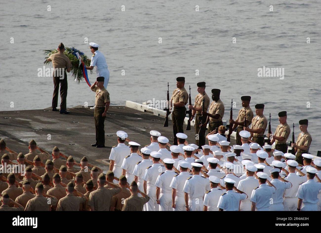 US Navy Sailors and Marines salute while a wreath is committed into the ...