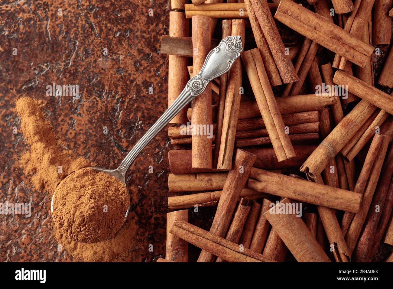 Cinnamon powder in a spoon and cinnamon sticks on a brown background ...