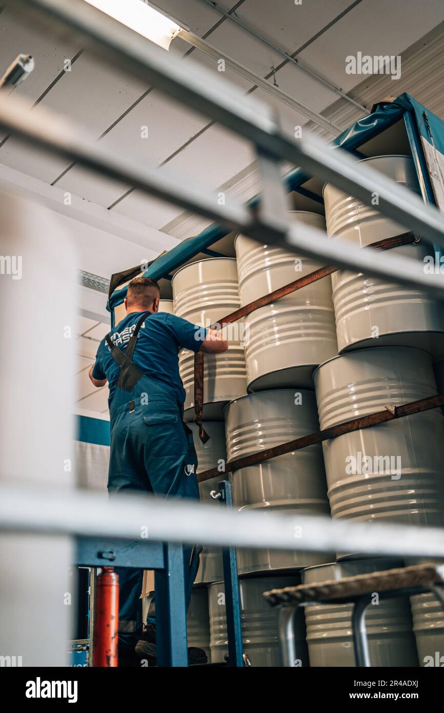 A worker seen from a low angle pushing multiple barrels of goods along ...
