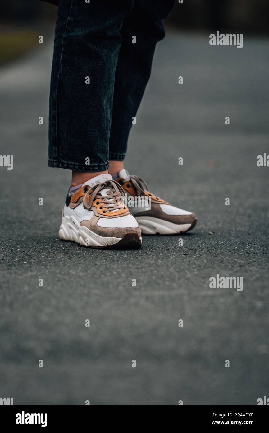 A person wearing sneakers standing on an urban street, their legs ...