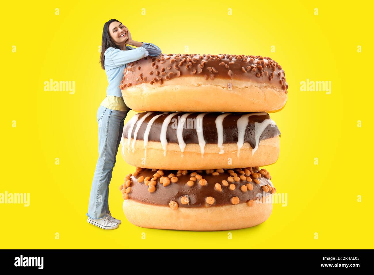 Happy young woman and stack of big donuts on yellow background Stock ...