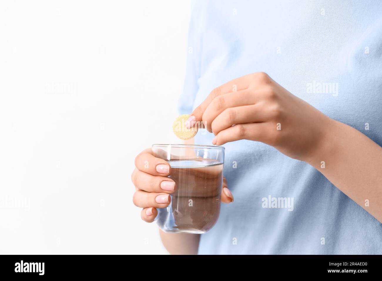 Woman putting soluble tablet into glass of water on white background ...