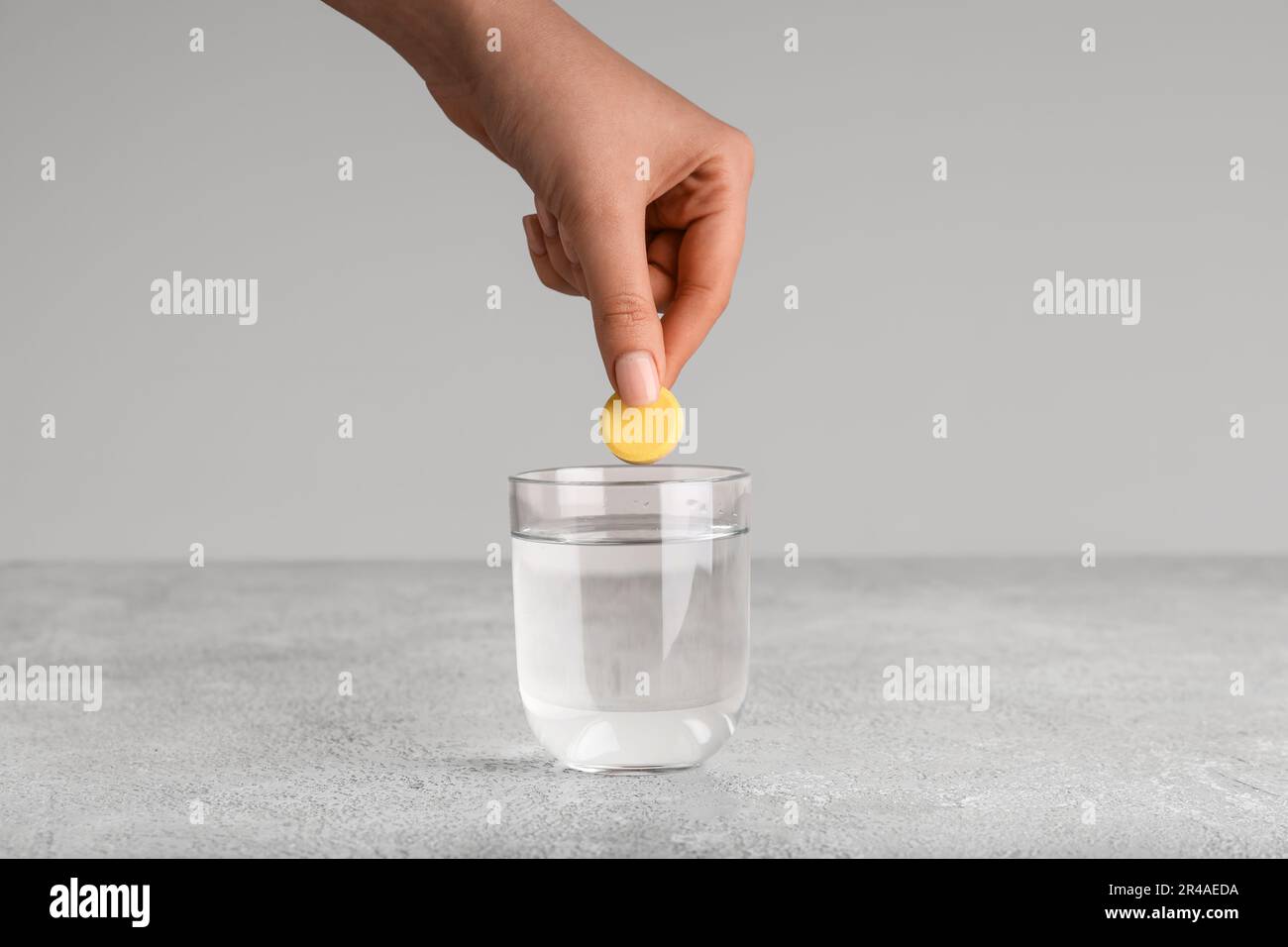Woman putting soluble tablet into glass of water on grey background ...