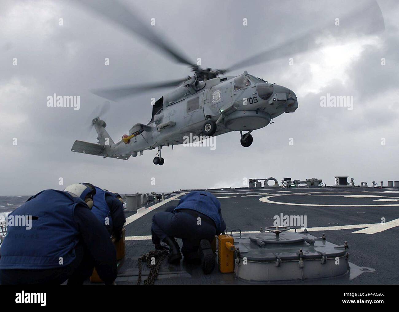 US Navy Sailors keep covered as an SH-60B Seahawk, assigned to the ...