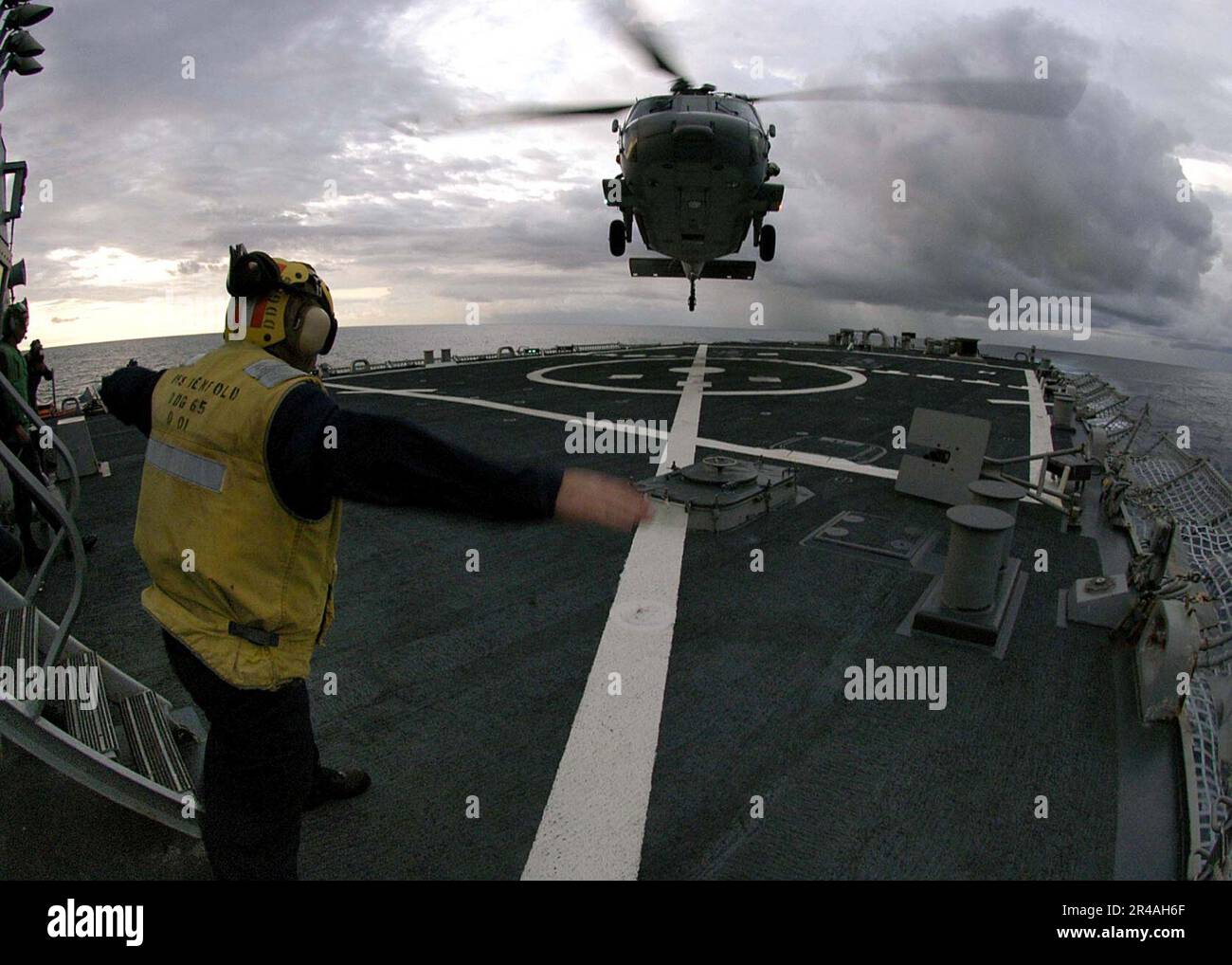 US Navy Boatswain's Mate 1st Class signals an MH-60S Knighthawk helicopter onto the flight deck ...