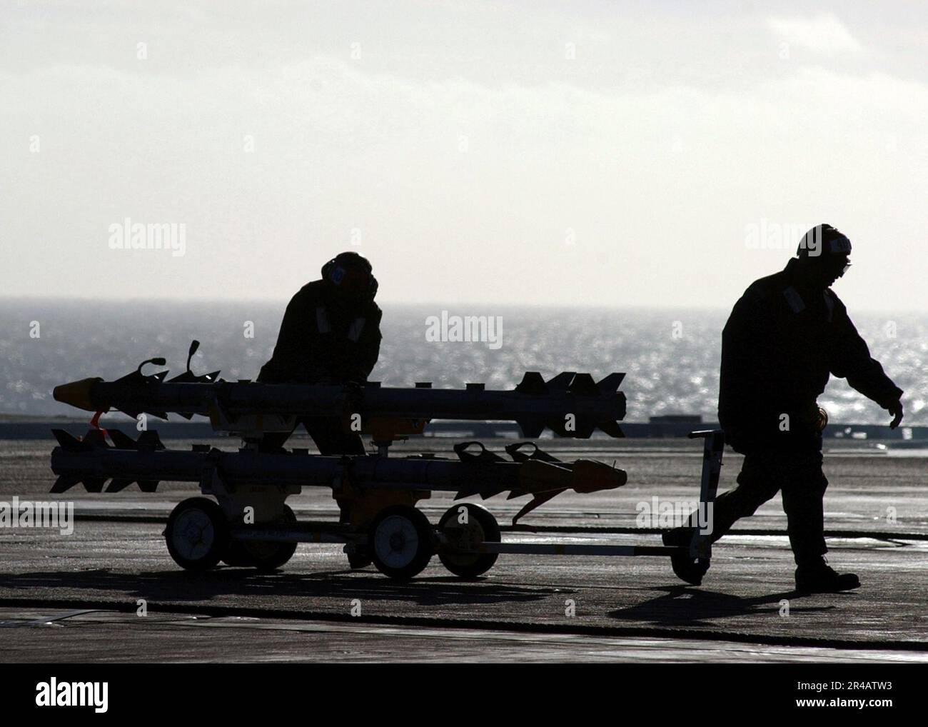 US Navy Two Aviation Ordnancemen transport a weapons cart loaded with ...