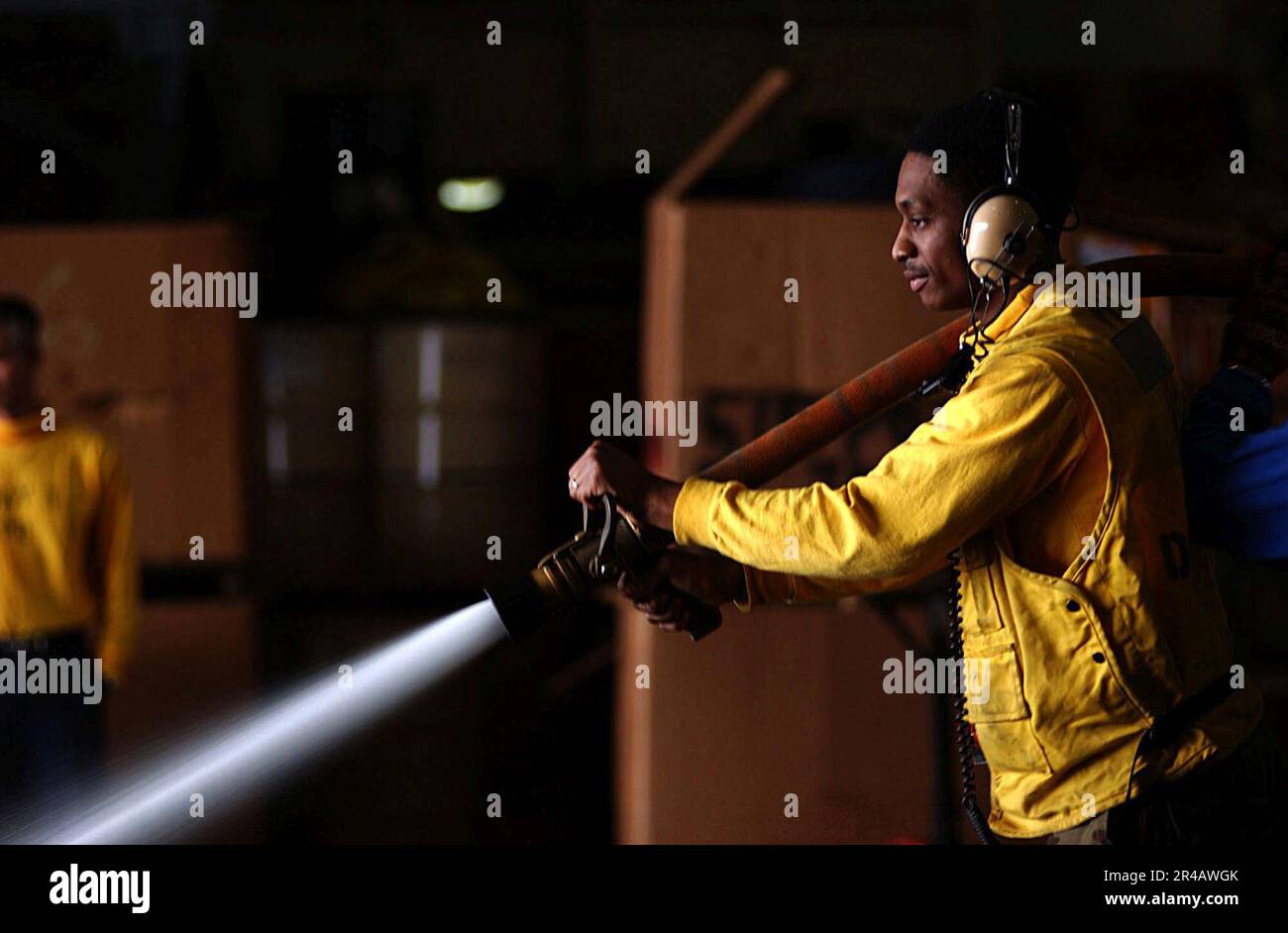 US Navy Airman uses a fire hose to soak the deck in a hangar bay ...