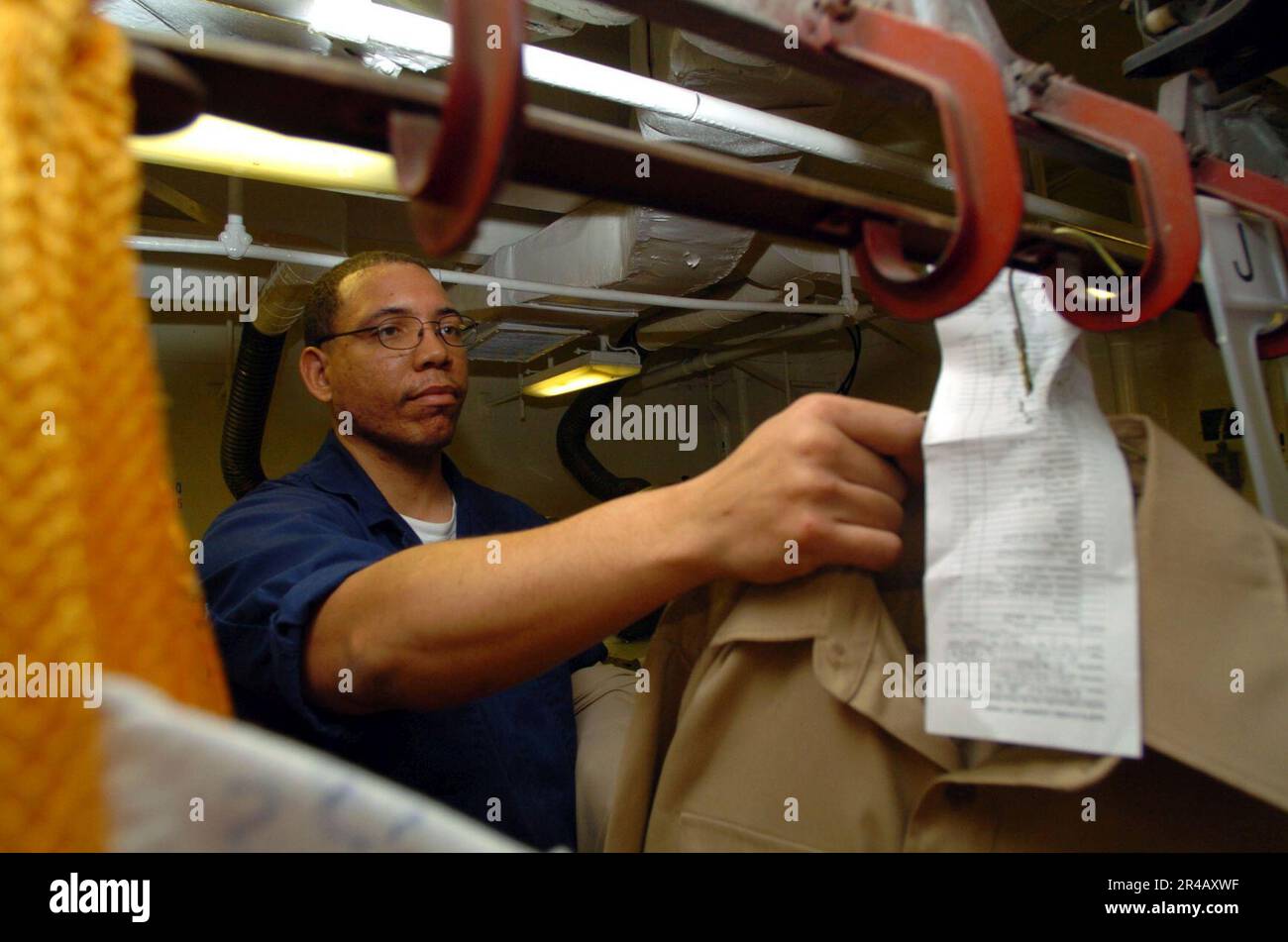 US Navy Airman hangs uniforms in Officer Issuing and Receiving aboard ...
