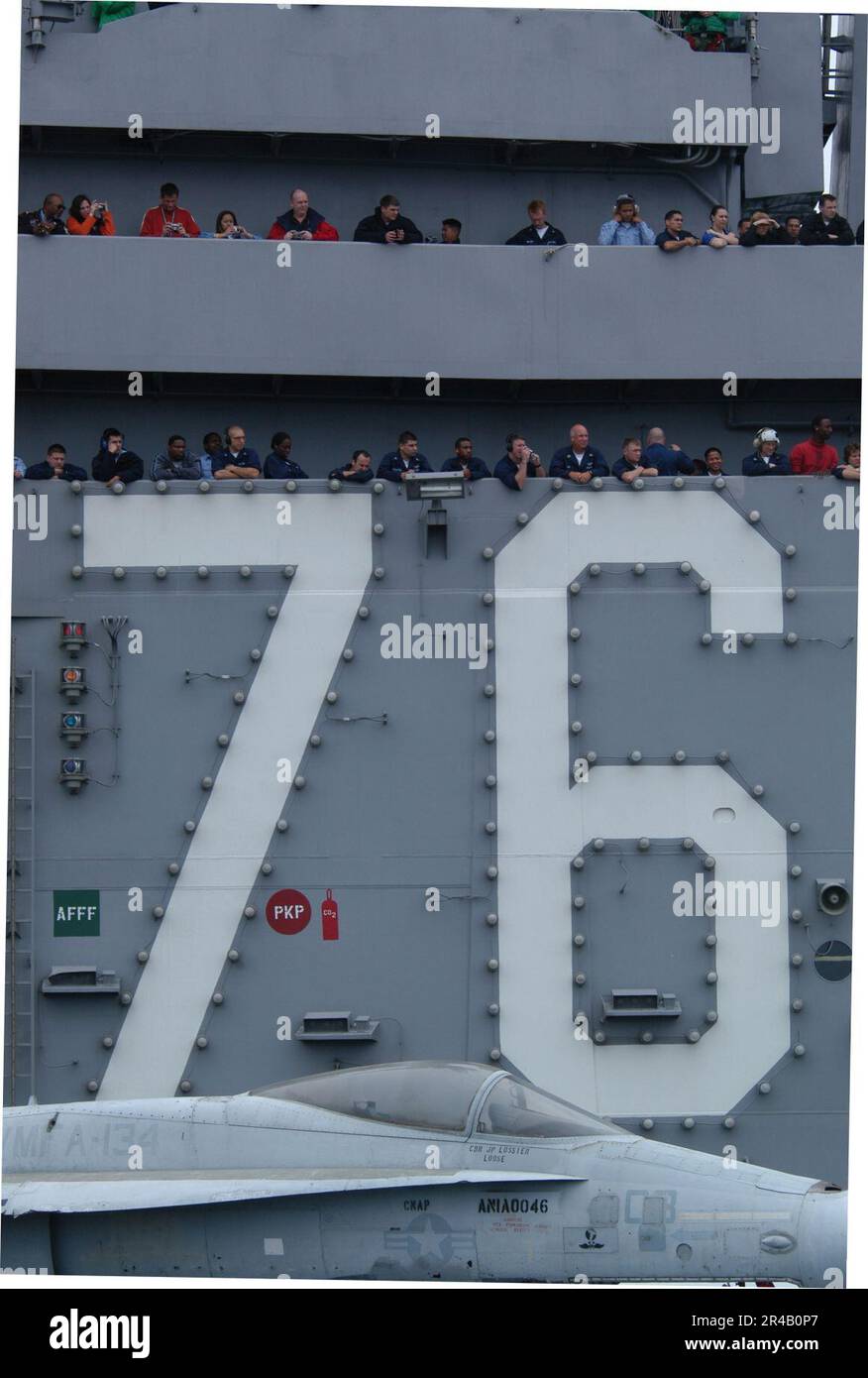 US Navy Crew members gather on the upper decks in the island to view a ...