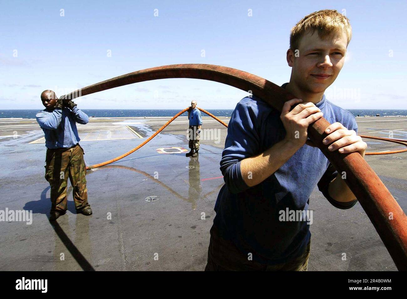 US Navy Three flight deck personnel hold the slack for a team ...
