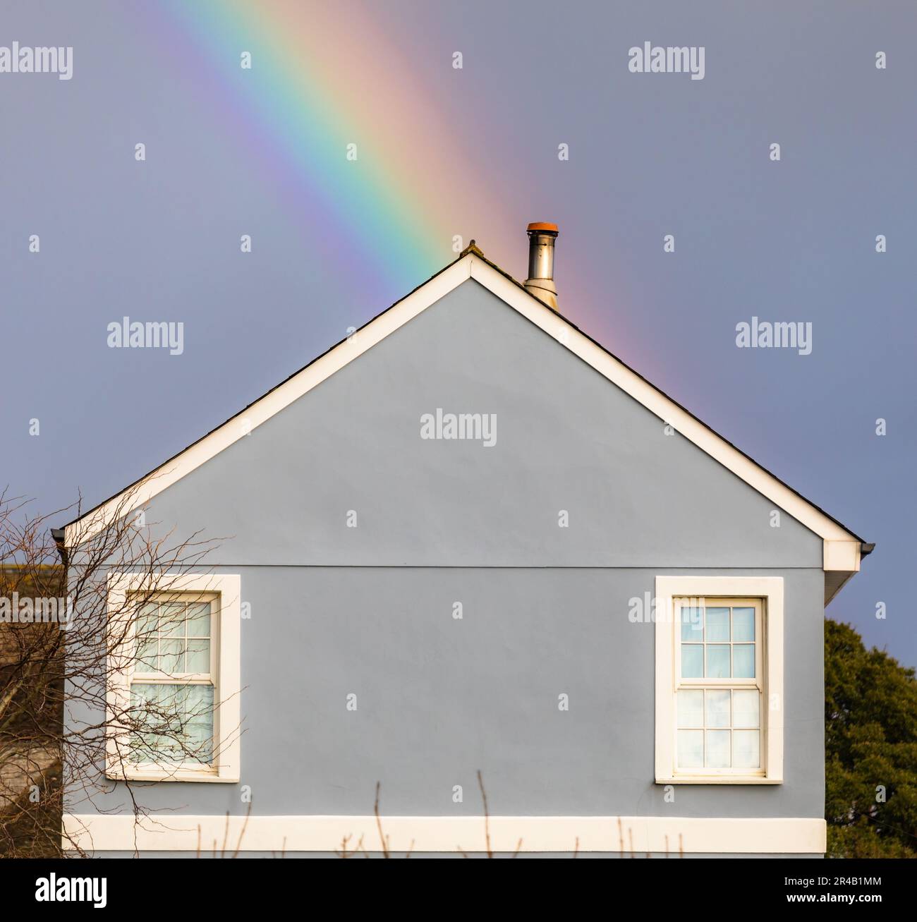 A vibrantly colorful rainbow illuminates a grey brick house, creating a ...