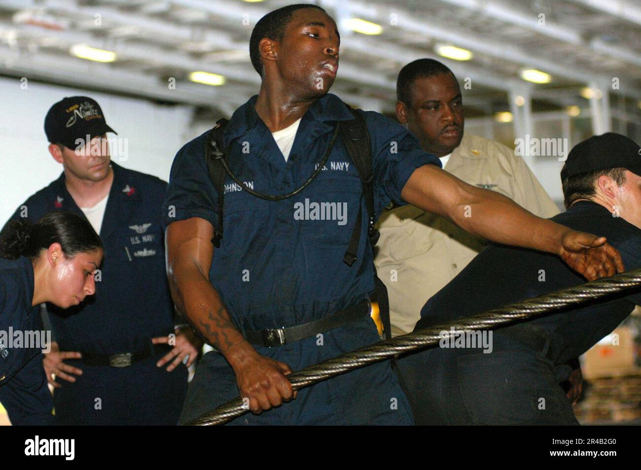 US Navy Airman pulls a new arresting gear cable out onto the hangar bay ...