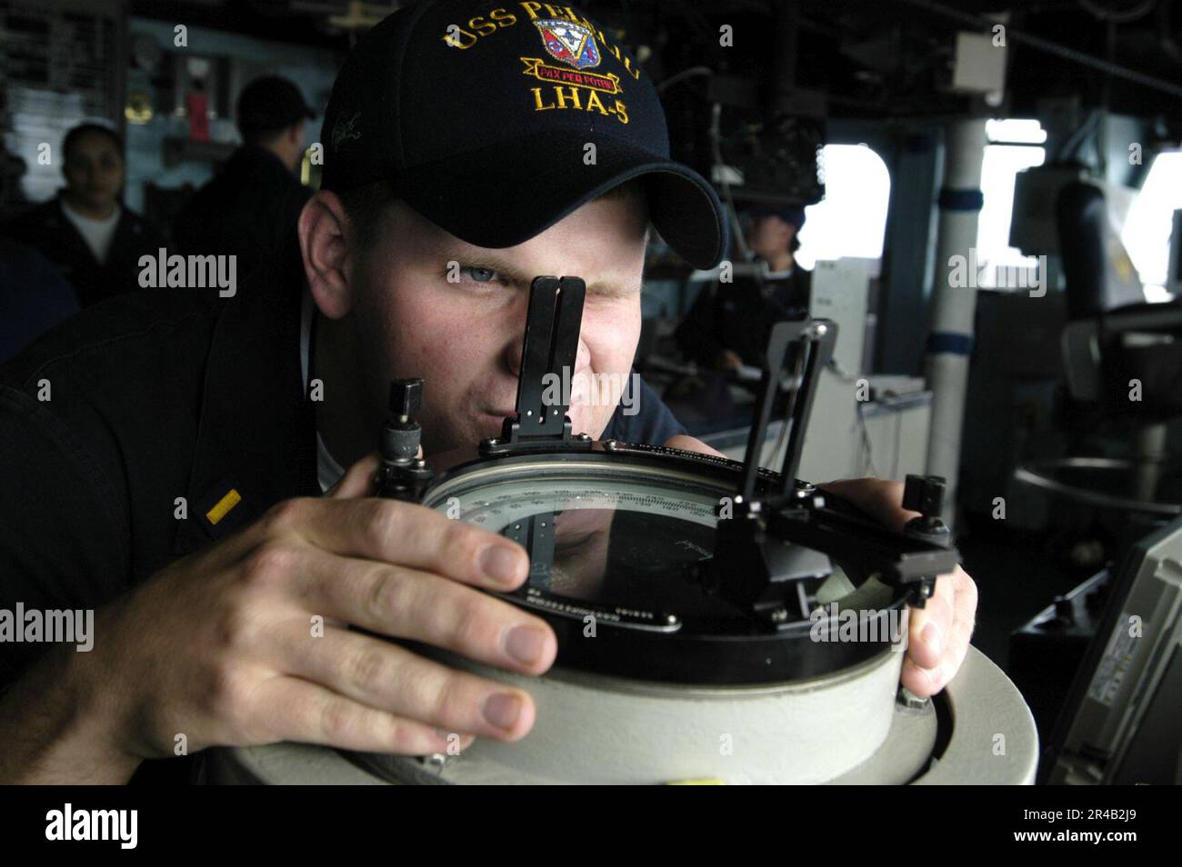 US Navy Junior Officer of the Deck (JOOD), Ens. uses the alidade on the bridge to take a bearing ...