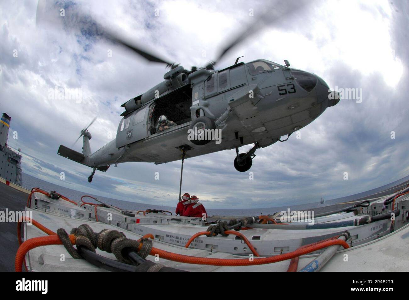 US Navy Aviation Ordnancemen hook a cargo pendant to an MH-60S Seahawk ...