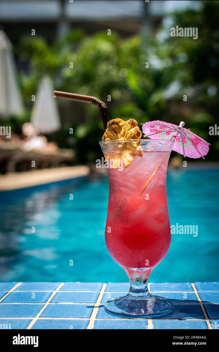 tropical singapore sling cocktail in tall glass by resort swimming pool ...