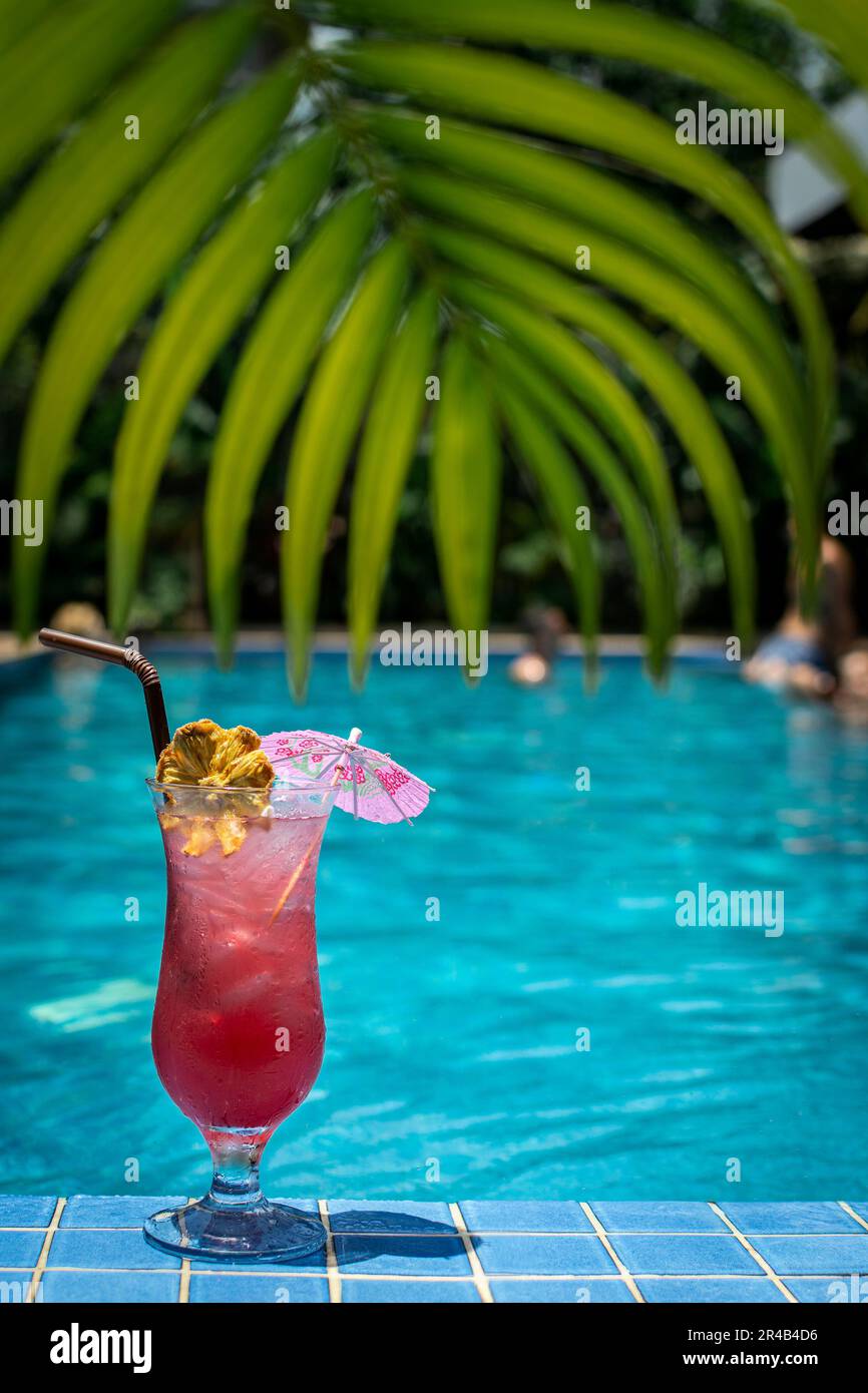 tropical singapore sling cocktail in tall glass by resort swimming pool ...