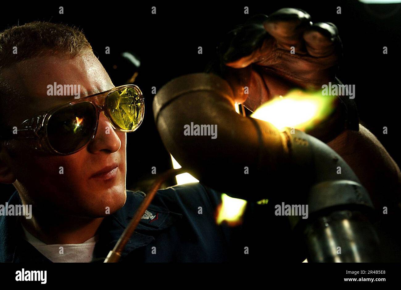 US Navy Hull Maintenance Technician 3rd Class braises a pipe fitting in ...