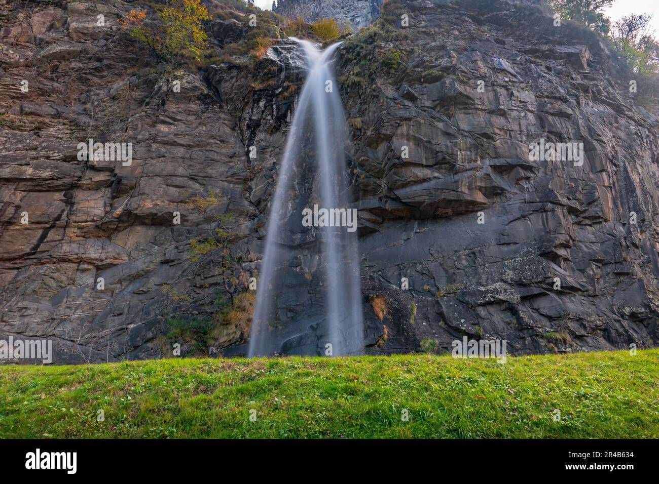 A cascading waterfall descends along a mountain cliff face, creating a ...