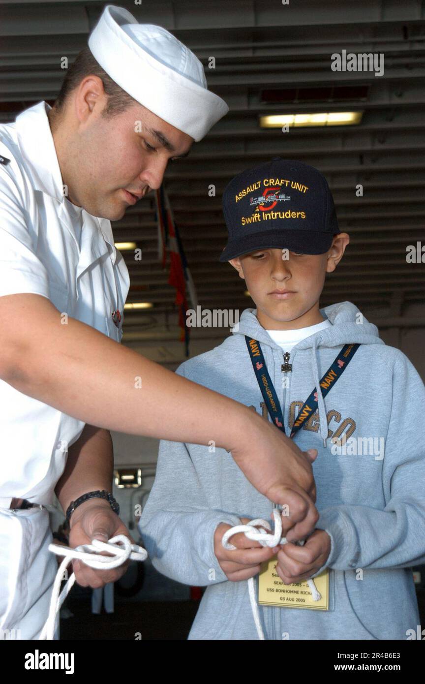 US Navy Seaman demonstrates the art of knot tying for a young embarked ...